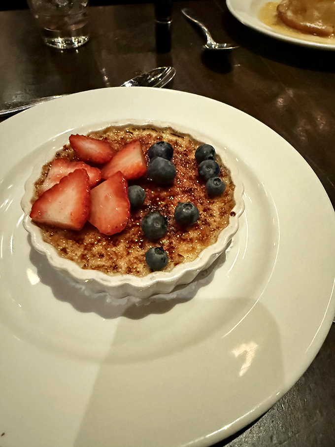Cr&egrave;me br&ucirc;l&eacute;e wears a crown of berries like jewels. The contrast between crisp caramelized sugar and cool creamy custard is culinary poetry.