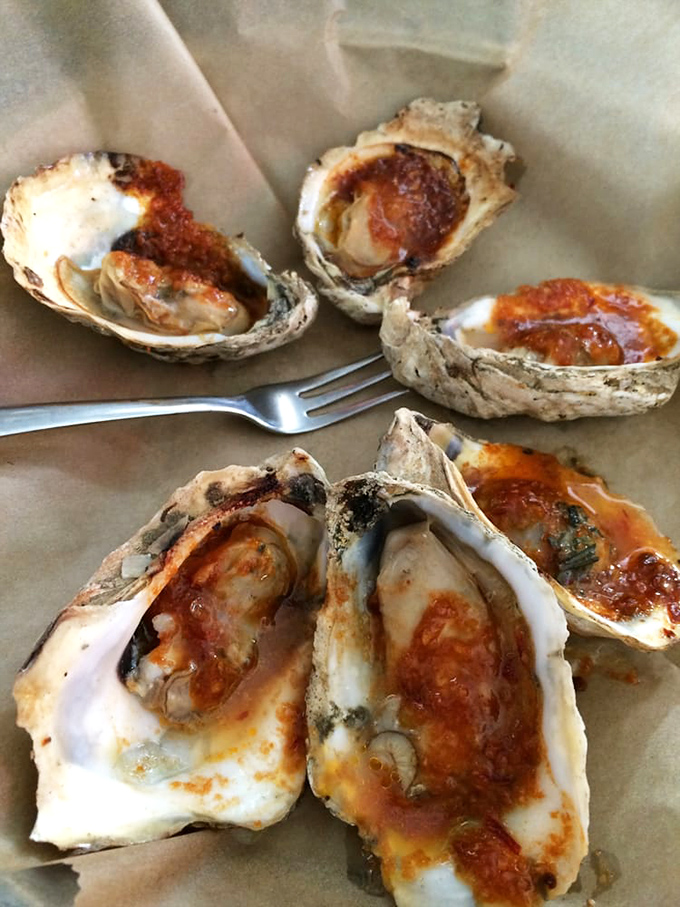 These aren't just grilled oysters&mdash;they're little boats of joy sailing on seas of savory sauce. The fork stands ready for the voyage of deliciousness that awaits.