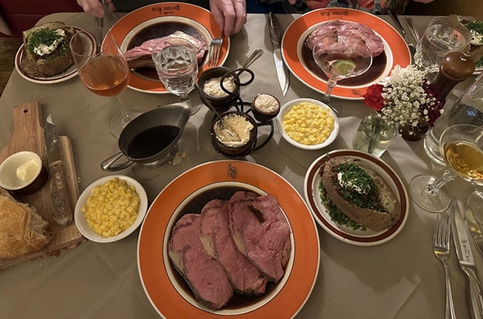 A table spread worthy of royalty: multiple cuts of prime rib, creamed corn, and baked potatoes loaded with all the good stuff life has to offer.