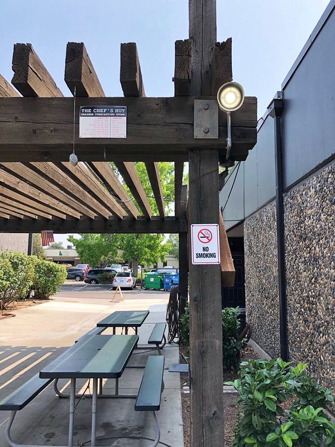 The outdoor seating area waits patiently under a rustic wooden pergola, offering fresh air with your fresh breakfast.