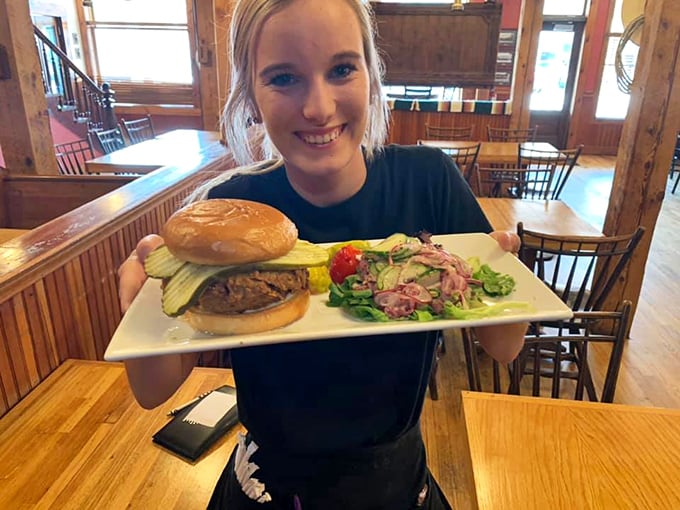 The server's smile is as genuine as the food is delicious, presenting a perfectly assembled burger plate with obvious pride.