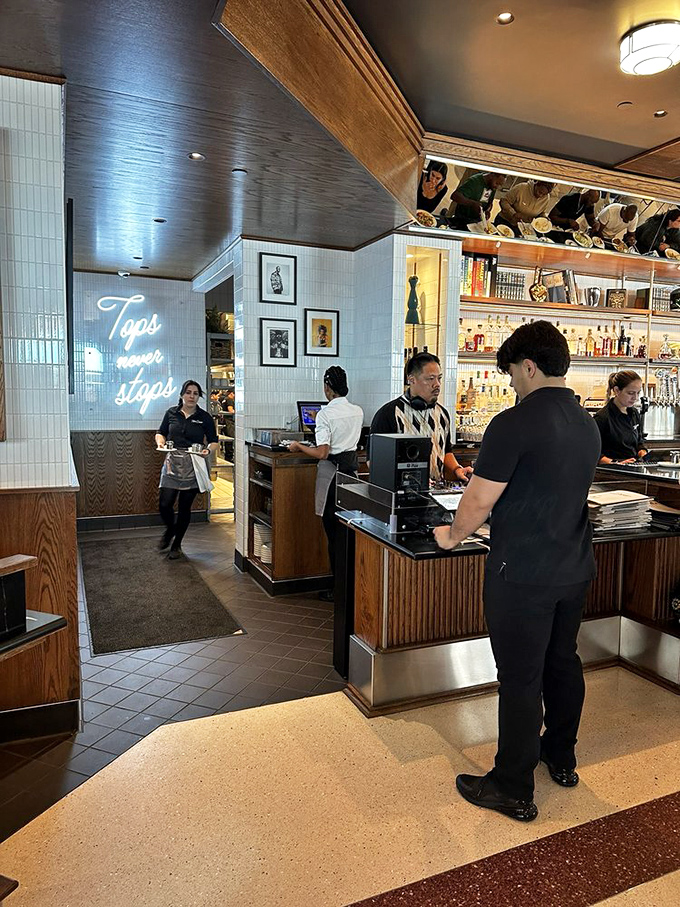 The "Tops Never Stops" neon sign illuminates the host station where the gatekeepers to breakfast paradise manage the hungry masses with clipboard efficiency.
