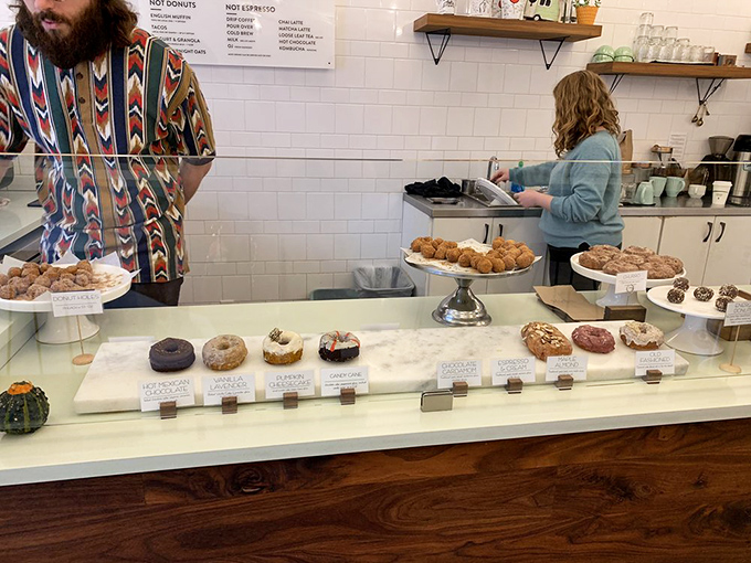 Behind marble counters, donut artisans arrange their circular masterpieces with the focused precision of gallery curators preparing for opening night.