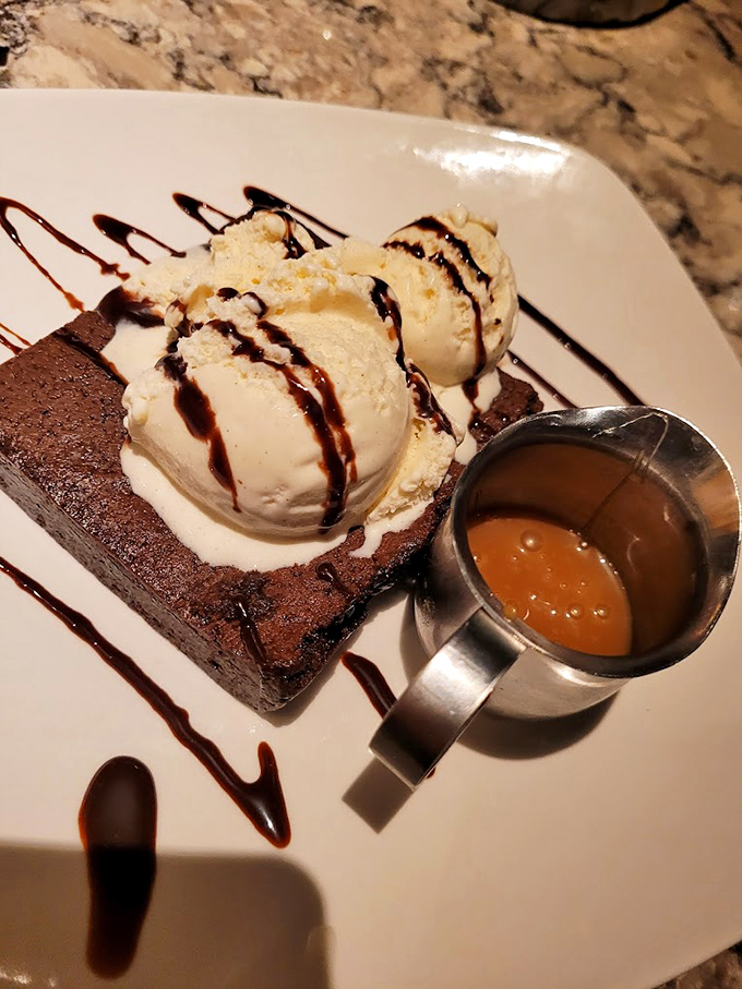 A brownie that deserves its own fan club, topped with ice cream and sauce. Dessert architecture that would make Frank Lloyd Wright weep.