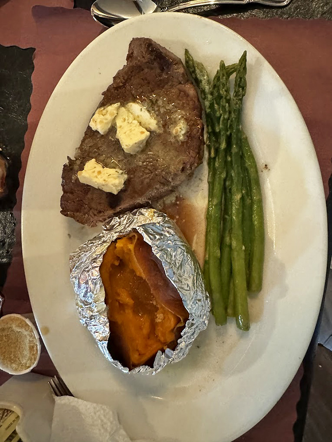 Steak topped with melting butter pats alongside asparagus spears and a sweet potato bundled like a precious gift. Simple perfection on a plate.