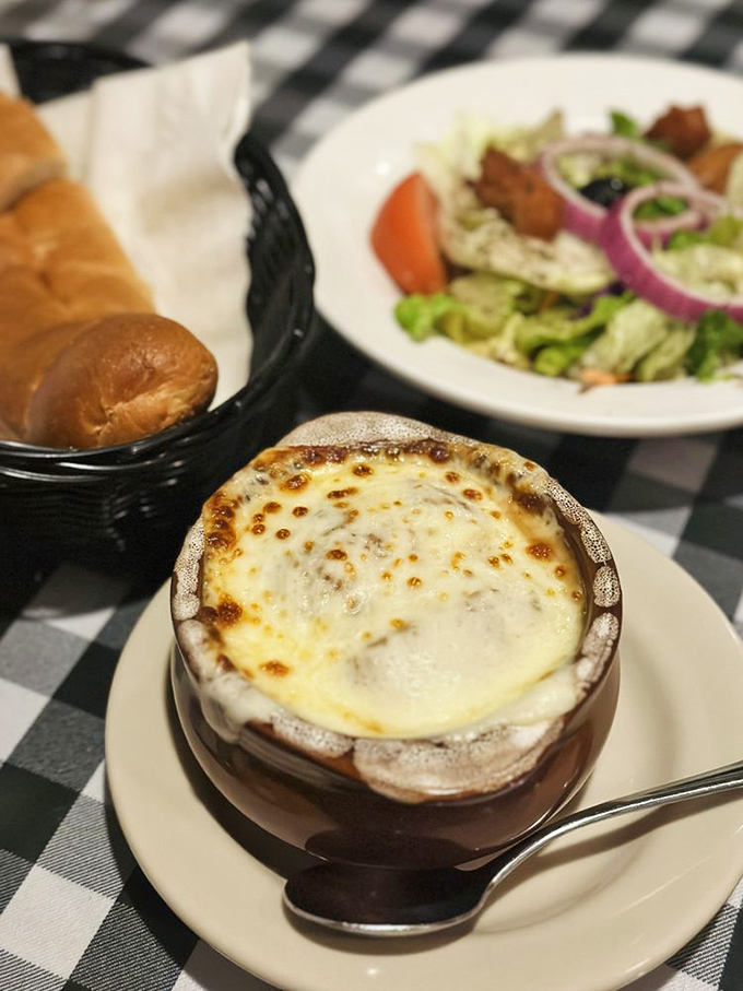 The French onion soup arrives like a bubbling cauldron of comfort, crowned with a golden dome of cheese that stretches dramatically with each spoonful.