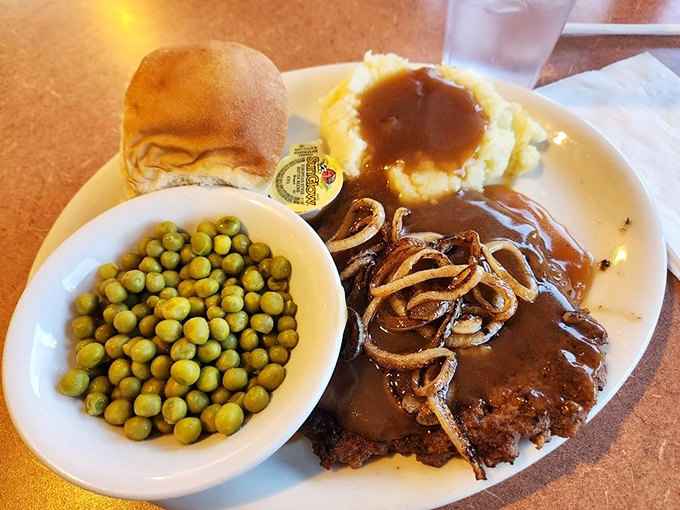 A hamburger steak that's gone formal with caramelized onions, gravy, and a side of peas that somehow makes this feel like a balanced meal.