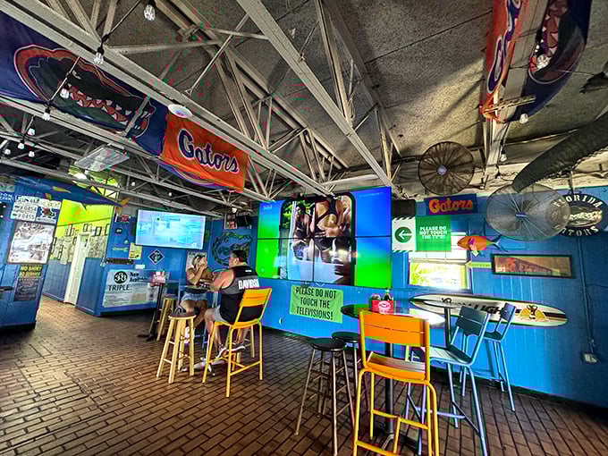Florida Gators flags hang proudly above colorful chairs. The sign warning "Please do not touch the televisions" suggests someone learned the hard way.er angle)