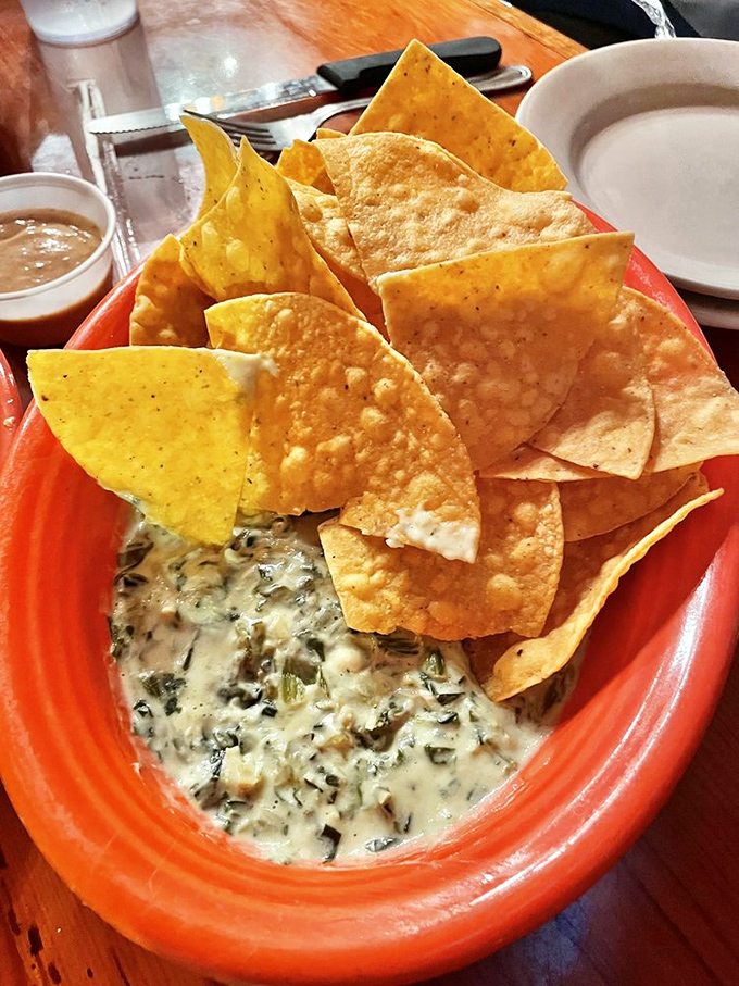 Spinach artichoke dip that doesn't apologize for its richness, surrounded by a defensive line of chips ready for the perfect scoop.