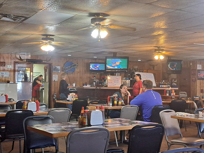 The interior reveals the wood-paneled charm of a place where the food speaks louder than the decor. Ceiling fans keep the air moving while TVs keep the conversation flowing.