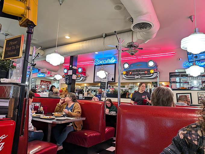 Red booths cradle conversations between strangers and old friends alike, while neon casts its rosy glow over plates of morning comfort.