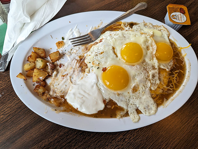 Three sunny-side-up eggs stand guard over a kingdom of potatoes and green chili &ndash; breakfast royalty that demands respect and multiple napkins.
