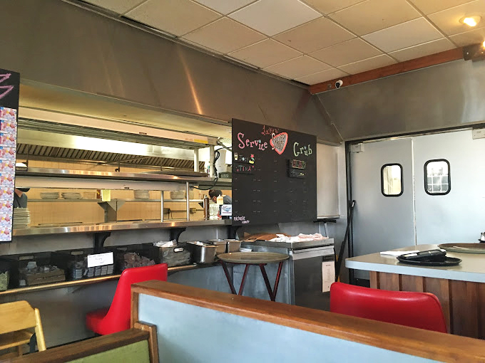 Behind the scenes where short-order symphonies are composed. That "Service with Care" sign isn't just decoration&mdash;it's the kitchen constitution.