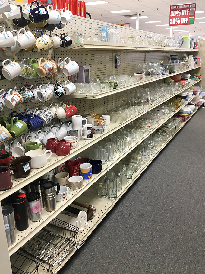 Coffee mugs hang like colorful fruit from a pegboard tree, while glassware gleams on shelves below. Your kitchen's missing pieces await!