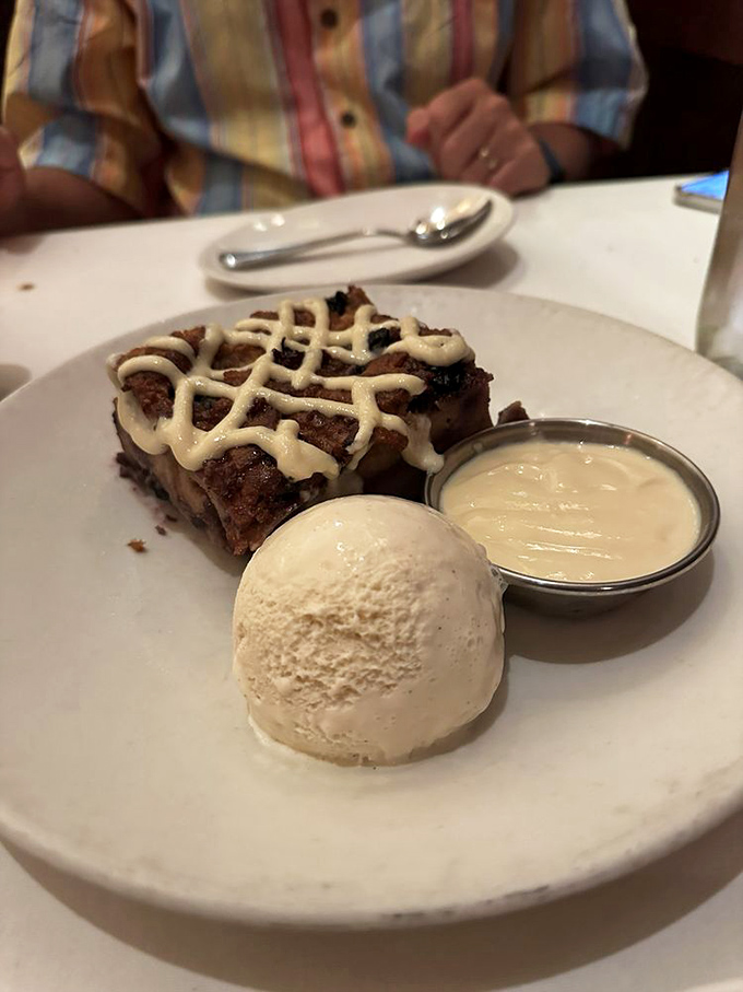 Bread pudding with a drizzle of sauce and ice cream on the side. The perfect sweet ending that makes you forget you just ate your weight in steak.