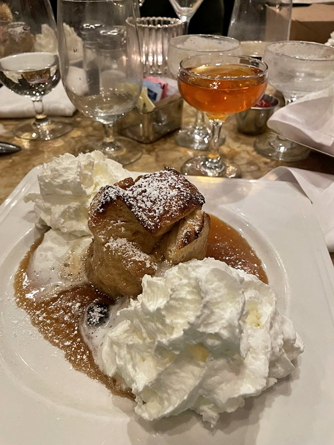 Bread pudding ascends to celestial heights when crowned with powdered sugar, surrounded by caramel pools, and flanked by whipped cream sentinels.