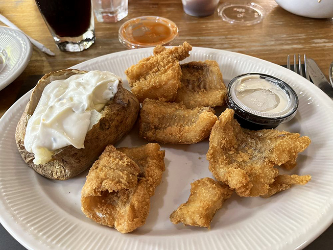 Fried Alaskan cod with a golden crust that shatters like delicate glass, paired with a baked potato wearing a cloud of sour cream.