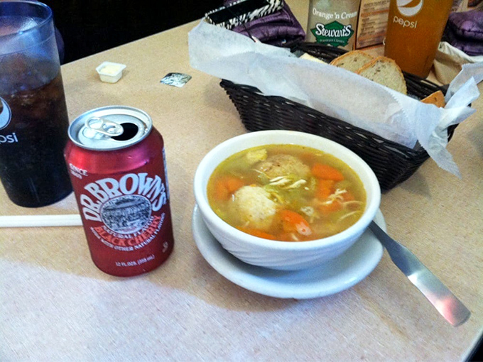 A steaming bowl of matzo ball soup alongside Dr. Brown's soda&mdash;the perfect supporting actors to Jake's sandwich star.