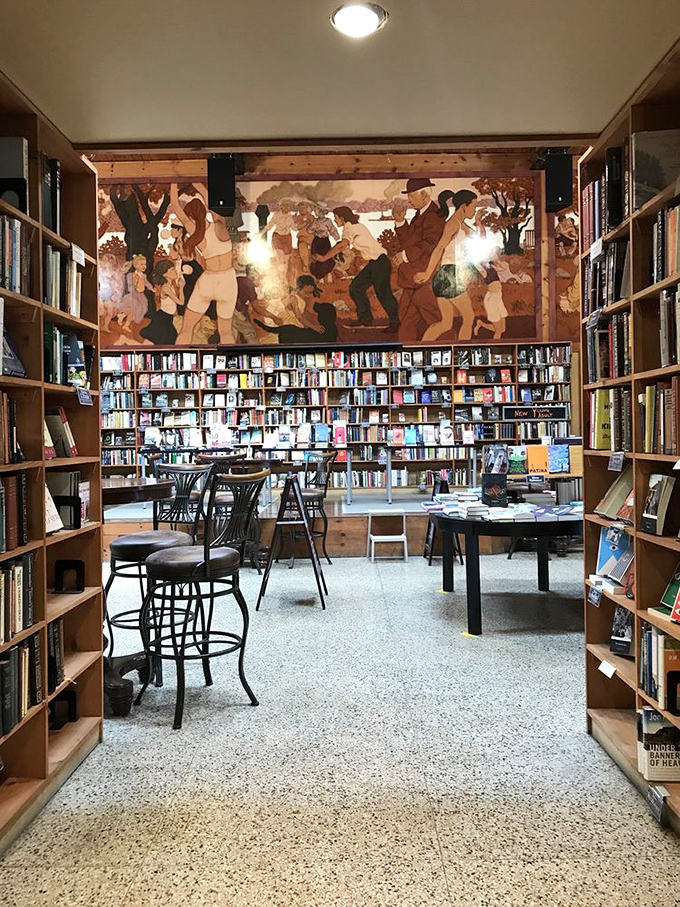 Art meets literature beneath warm wooden beams. The stunning mural overlooking the reading area captures the vibrant cultural heart of this bookish haven.