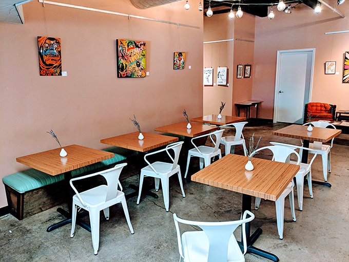 Minimalist charm meets artistic soul in this airy space where wooden tables, white chairs, and vibrant local art create the perfect donut-contemplation environment.