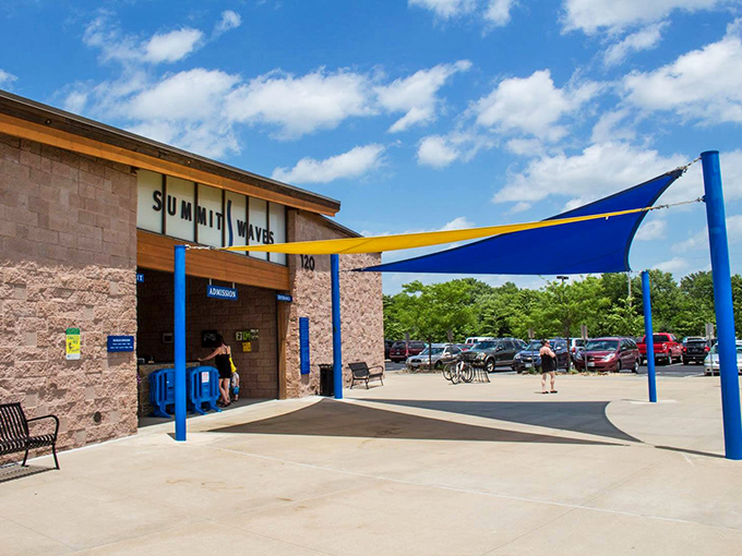 The welcoming entrance to Summit Waves stands ready for summer escapees, its stone facade and blue awning like a portal to a chlorinated paradise.