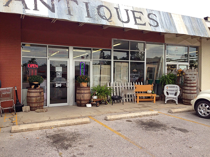 The entrance says it all – wooden barrels, rustic benches, and that weathered "ANTIQUES" sign promising adventures in nostalgia just beyond those doors.