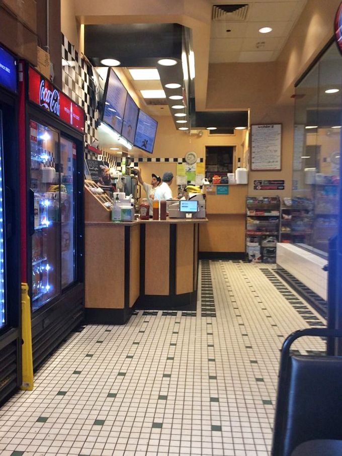 Behind that counter, sandwich artisans perform their daily ritual of stacking, slicing, and serving deli perfection against a classic checkerboard backdrop.
