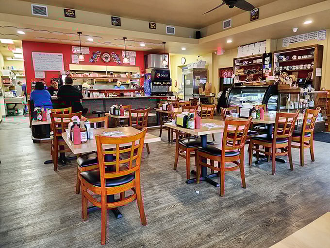 Inside, wooden tables and chairs create that perfect small-town diner atmosphere where conversations flow as freely as the coffee. The red accent wall adds warmth to this cozy gathering spot.