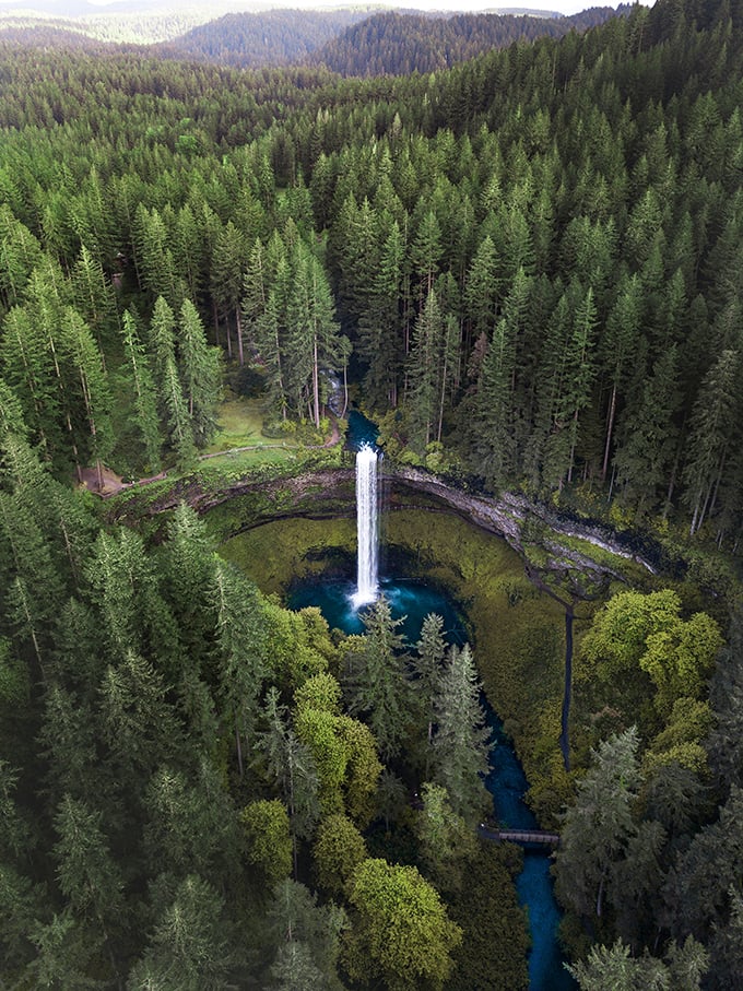 From above, this waterfall looks like Mother Nature dropped a perfect sapphire into an emerald setting. The blue pool practically glows against the surrounding forest.