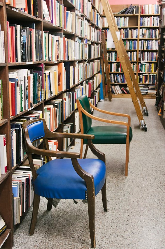Literary canyons formed by towering shelves, with comfortable chairs inviting you to sit and sample. The wooden ladder isn't decorative&mdash;it's an essential exploration tool.