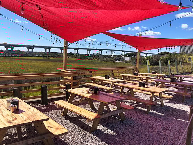 Red sail shades and picnic tables create the perfect casual backdrop for serious seafood enjoyment, with the Surf City bridge framing the view.