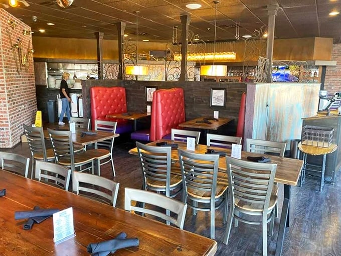 Red tufted booths stand like culinary thrones amid rustic wood tables, where brick walls and open ceilings create the perfect backdrop for flavor revelations.