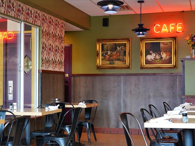 The cozy interior balances retro charm with modern comfort, where the glowing "CAFE" sign serves as a beacon for breakfast pilgrims seeking morning salvation.