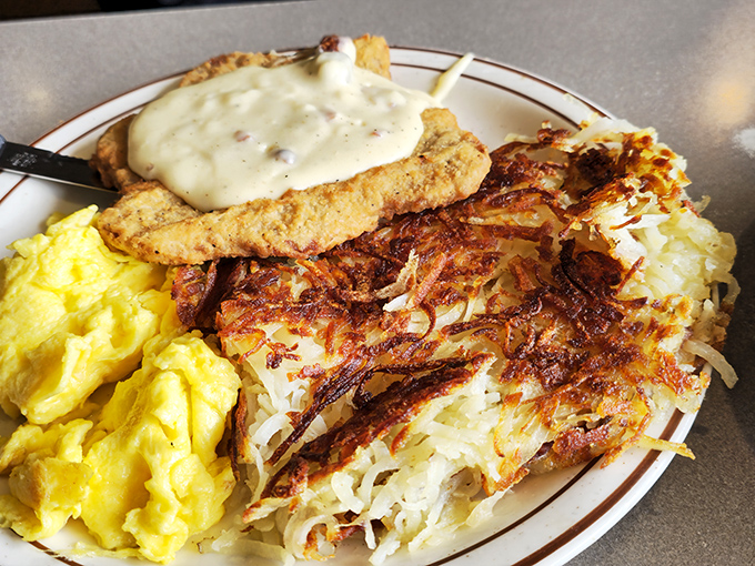 Behold, the holy trinity of breakfast: golden eggs, crispy hash browns, and chicken fried steak swimming in gravy. Morning salvation on a plate.