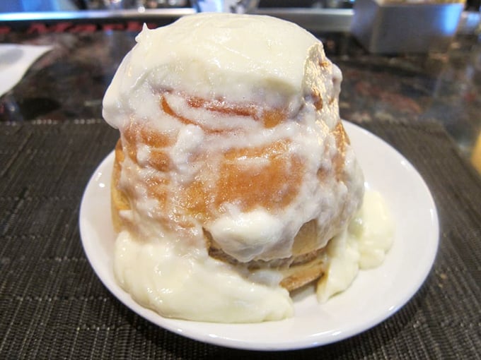The legendary cinnamon roll arrives like a frosting-capped mountain of joy—a sugary Everest worth every calorie-burning expedition afterward.