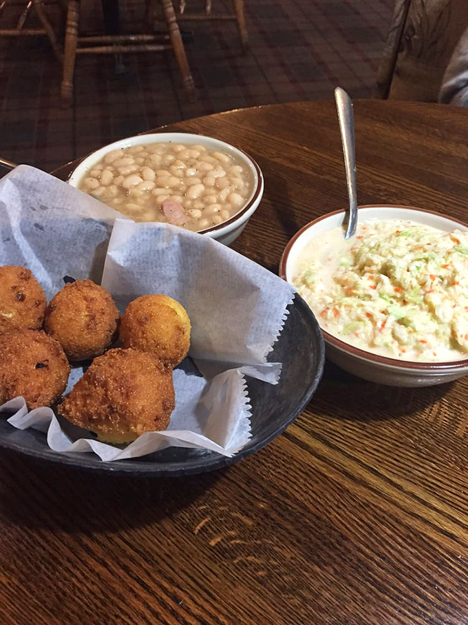 Golden hush puppies nestled in paper, flanked by creamy coleslaw and beans with ham. The holy trinity of Southern sides that completes any proper catfish feast.