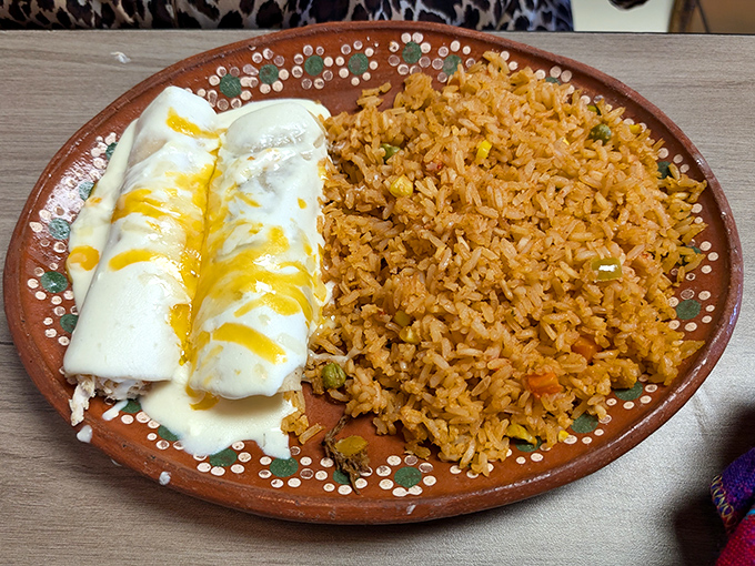 Two pristine enchiladas draped in cheese sauce recline on a hand-painted clay plate beside Spanish rice that's practically doing the maracas.