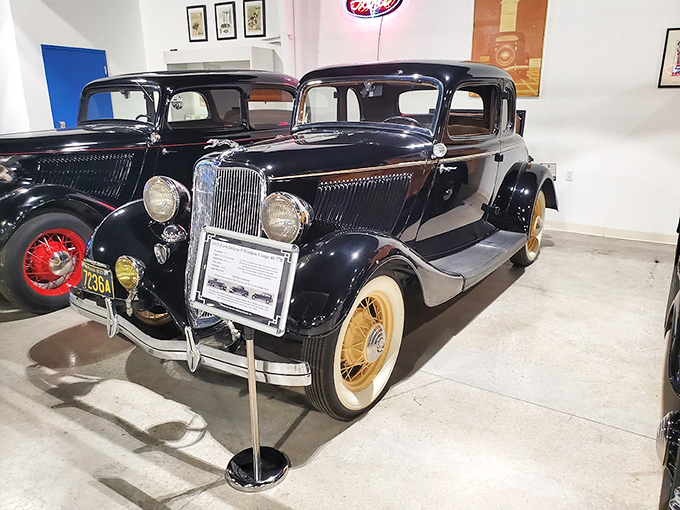 The elegant black Ford Deluxe 5-window coupe sits regally with its red-accented wheels, representing an era when cars weren't just vehicles but works of art.