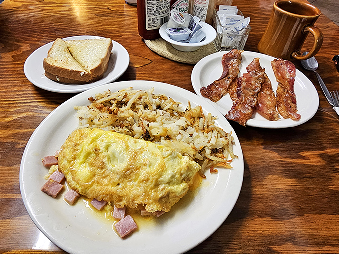 Behold the holy trinity of breakfast: a perfectly folded omelet, crispy-edged hash browns, and bacon that would make even vegetarians question their life choices.