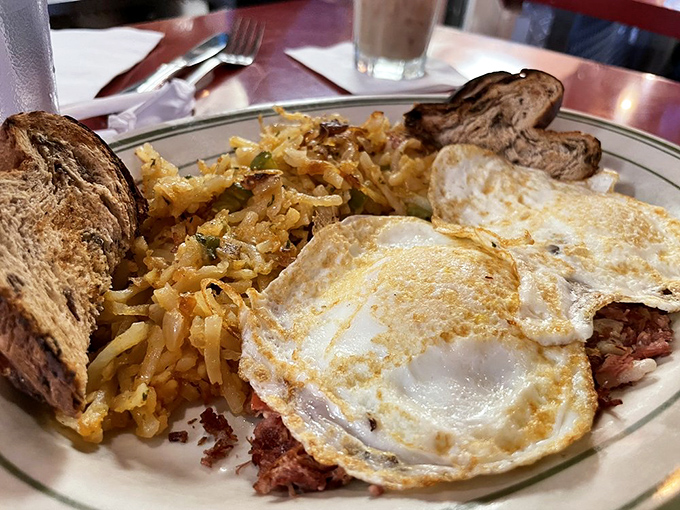 Breakfast nirvana: crispy home fries, perfectly fried eggs, and corned beef hash creating a holy trinity of morning satisfaction.