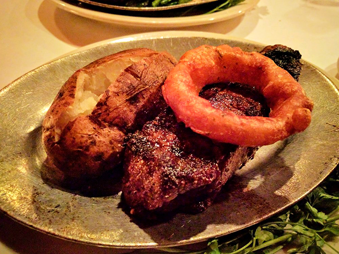 A perfectly seared steak alongside a loaded baked potato and crispy onion ring&mdash;the holy trinity of Wisconsin steakhouse bliss.