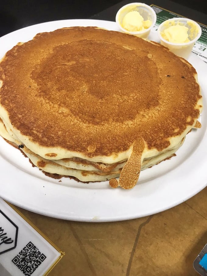 Behold the pancake stack that launched a thousand road trips. Golden-brown perfection with two cups of butter standing by like loyal sidekicks.