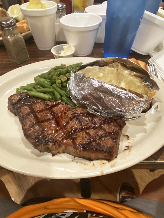 A perfectly grilled ribeye with green beans and a foil-wrapped potato&mdash;the holy trinity of steakhouse satisfaction. Meat poetry on a white plate.