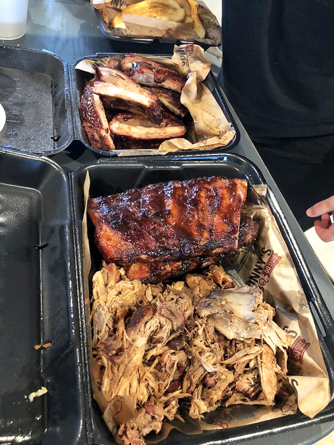 Barbecue nirvana in black plastic containers—where pulled pork and ribs coexist in smoky harmony like the best kind of family reunion.