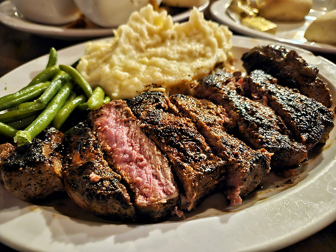 The medium-rare ribeye arrives like edible artwork&mdash;charred exterior giving way to a ruby center, flanked by creamy mashed potatoes and vibrant green beans.
