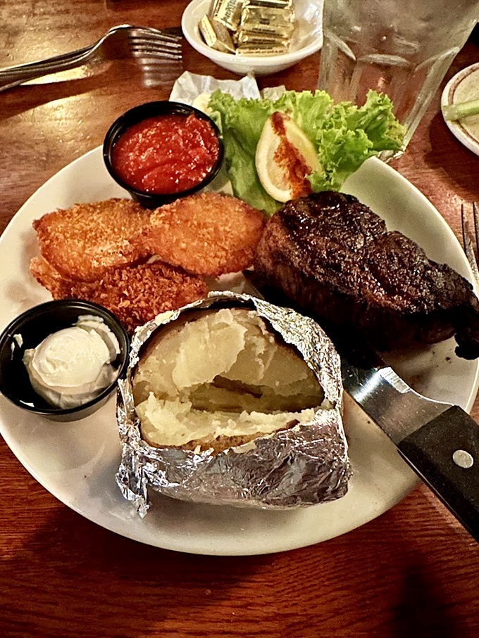 The holy trinity of steakhouse perfection: a perfectly seared cut, a loaded baked potato, and that little cup of sauce you'll be tempted to drink.
