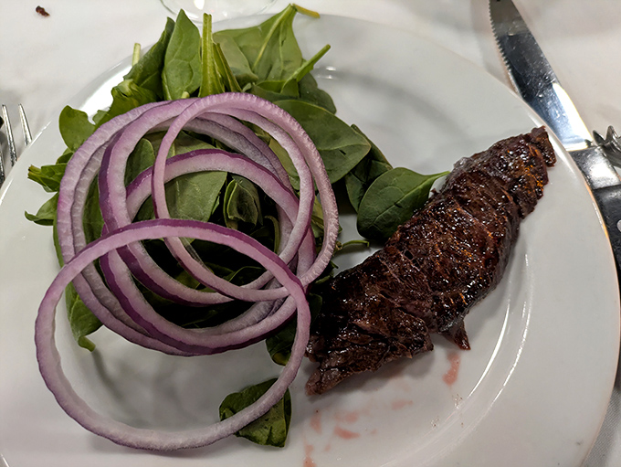 A perfectly seared steak strip lounges on crisp greens with red onion rings—like a protein superstar taking a well-deserved rest on a bed of vegetables.
