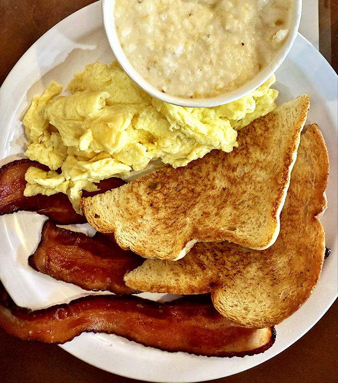 Breakfast perfection on a plate: golden toast, fluffy scrambled eggs, crispy bacon, and creamy grits that would make any Southerner proud.