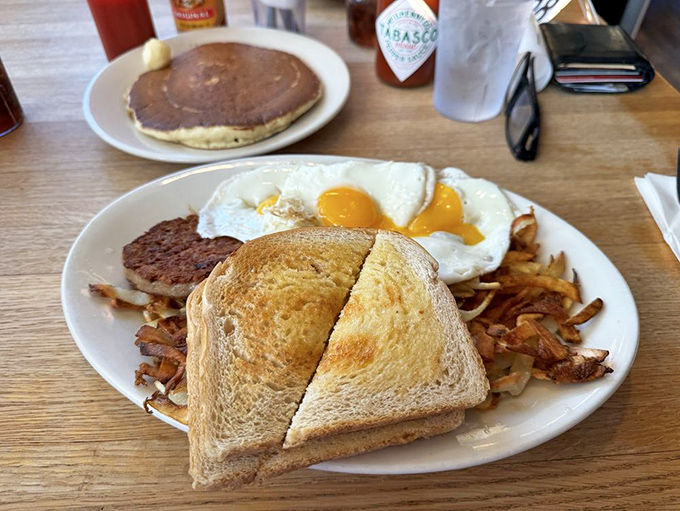 The breakfast trinity: perfectly sunny-side-up eggs, sausage with that satisfying snap, and hash browns crispy enough to make a potato proud. 