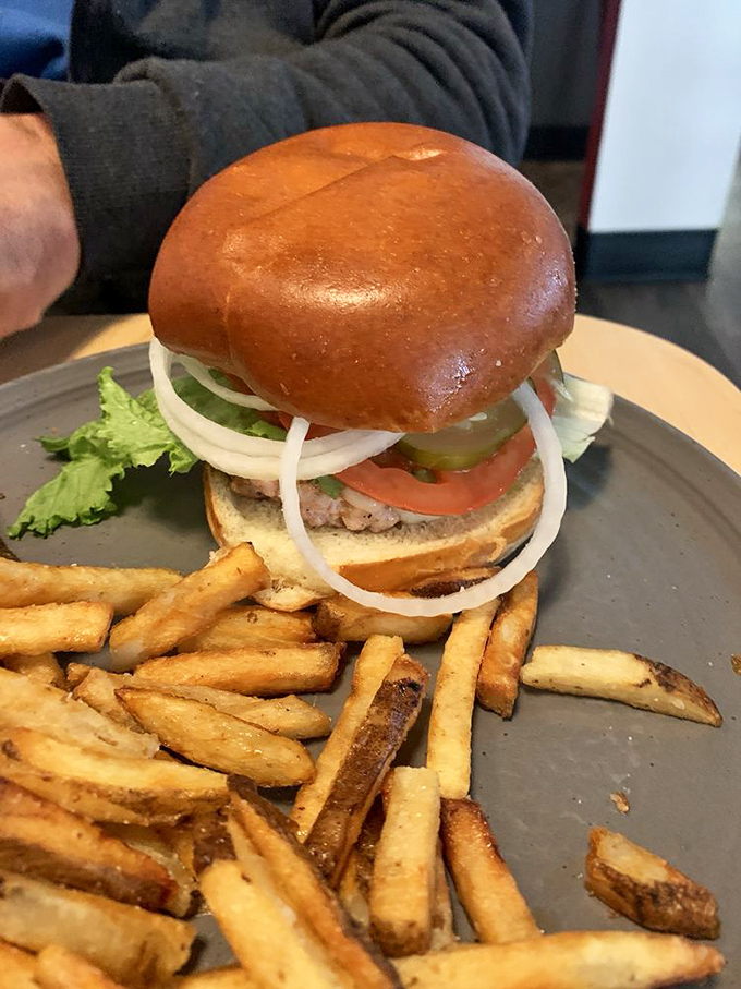 A classic burger in its natural habitat &ndash; perched atop golden fries, wearing its vegetables like medals of honor.